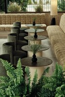 Uma área de estar moderna com sofá, várias mesas redondas e plantas em vasos.