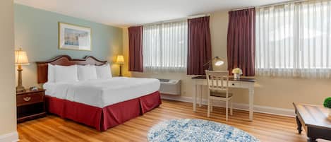 Quarto de hotel com cama, escrivaninha, cadeira e tapete redondo.