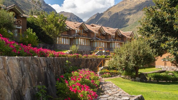 Um edifício tradicional com vários quartos, um caminho de pedra e um jardim com flores cor-de-rosa.