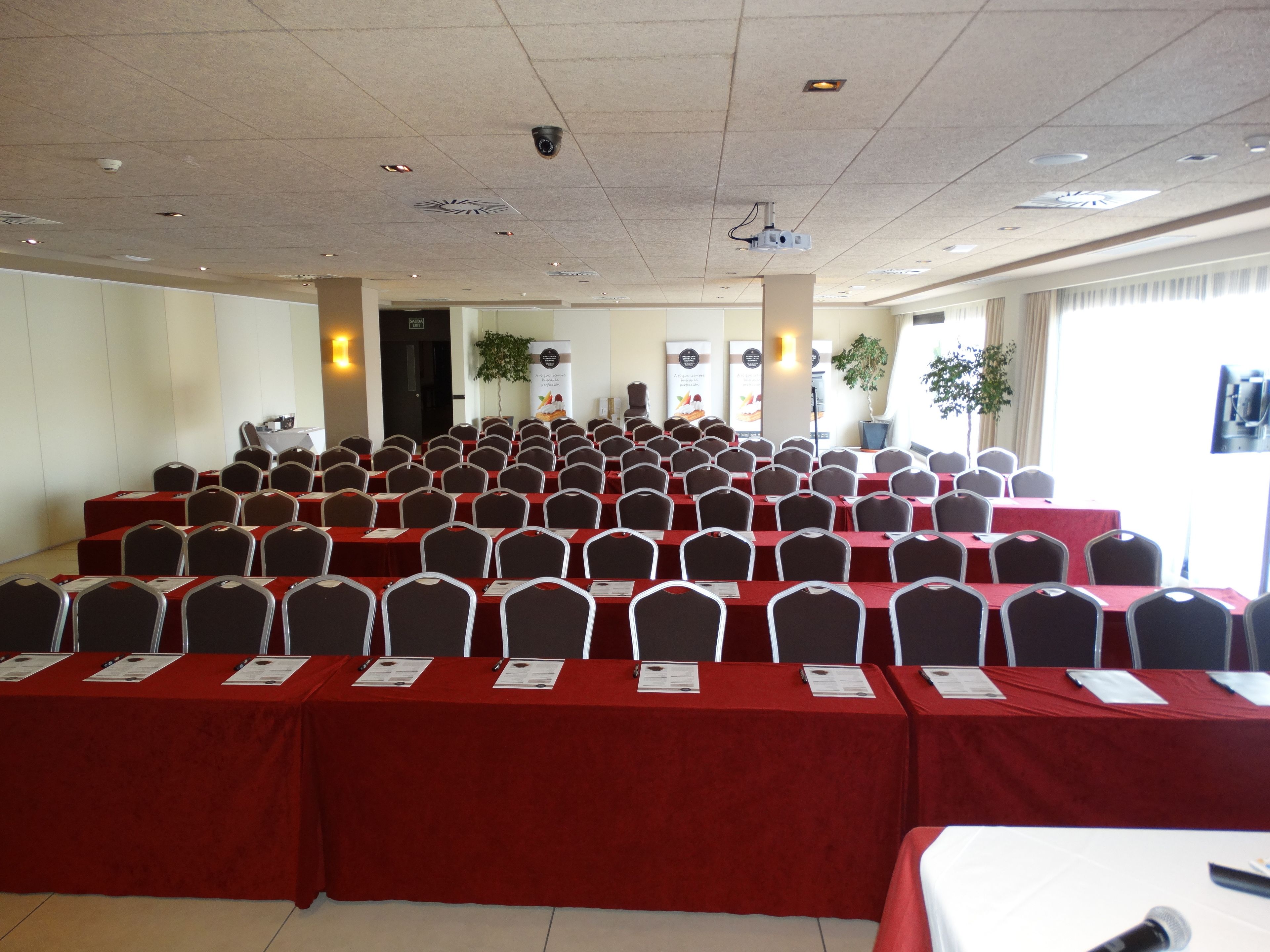 Uma sala de conferência com fileiras de mesas e cadeiras, equipada com microfones e placas de identificação.