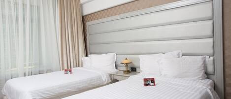 Quarto de hotel com duas camas de solteiro, mesa de cabeceira com abajur e uma janela grande com cortinas translúcidas.