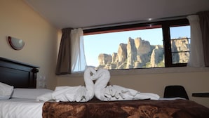 Quarto de hotel com cama, janela com cortinas e vista para formações rochosas.