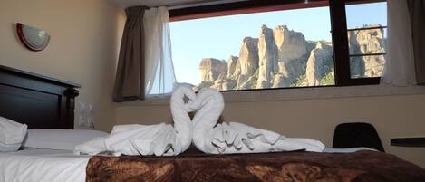 Quarto de hotel com cama, janela com cortinas e vista para formações rochosas.