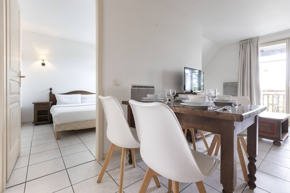 Quarto de hotel com uma cama, uma mesa de jantar com cadeiras, uma televisão e uma janela com cortinas.