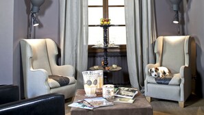 Uma sala de estar aconchegante com teto alto, dois poltronas, uma mesa de centro com revistas e uma janela com cortinas.