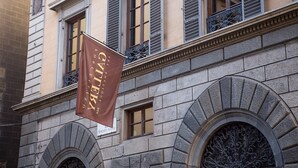 Fachada de um edifício com paredes de pedra, janelas em arco e uma placa pendurada.