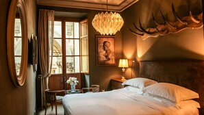 Quarto de hotel com cama, lustre, cabeça de animal montada, pintura e janela com cortinas.