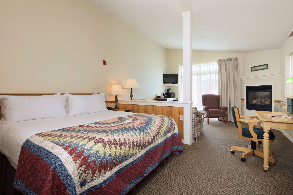 Quarto de hotel com uma cama grande, uma escrivaninha, uma cadeira, uma televisão e uma lareira.
