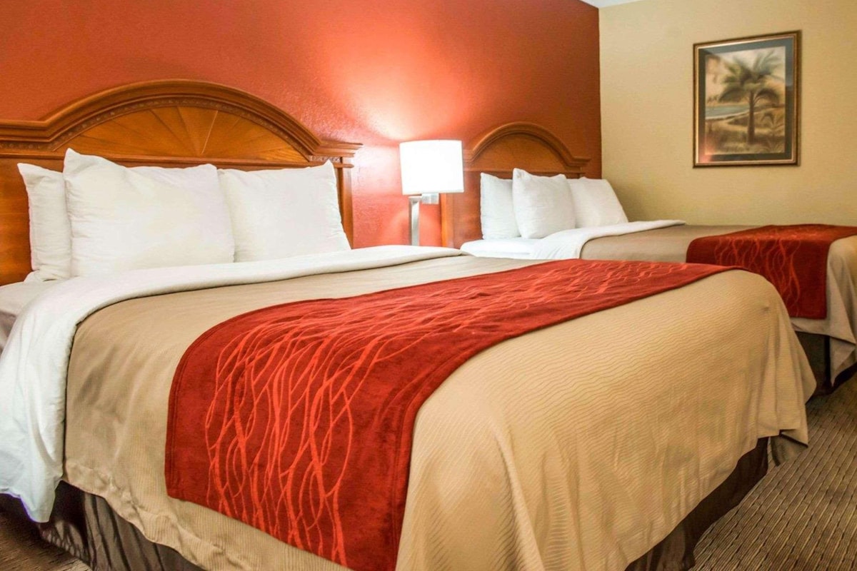 Quarto de hotel com duas camas, cada uma com roupa de cama branca e um toque de vermelho.