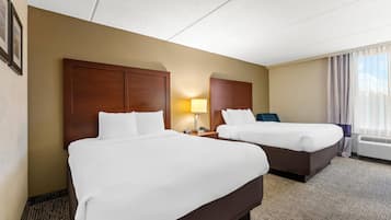 Quarto de hotel com duas camas, uma mesa de cabeceira, um abajur e uma janela com cortinas.