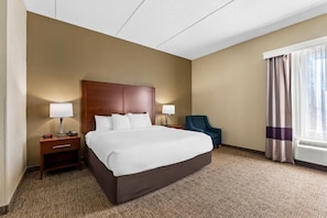 Quarto de hotel com uma cama grande, duas mesas de cabeceira com luminárias, uma cadeira e uma janela com cortinas.