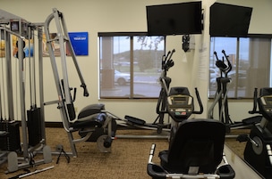 Uma academia com diversos equipamentos de exercício, uma janela grande e um cartaz motivacional na parede.