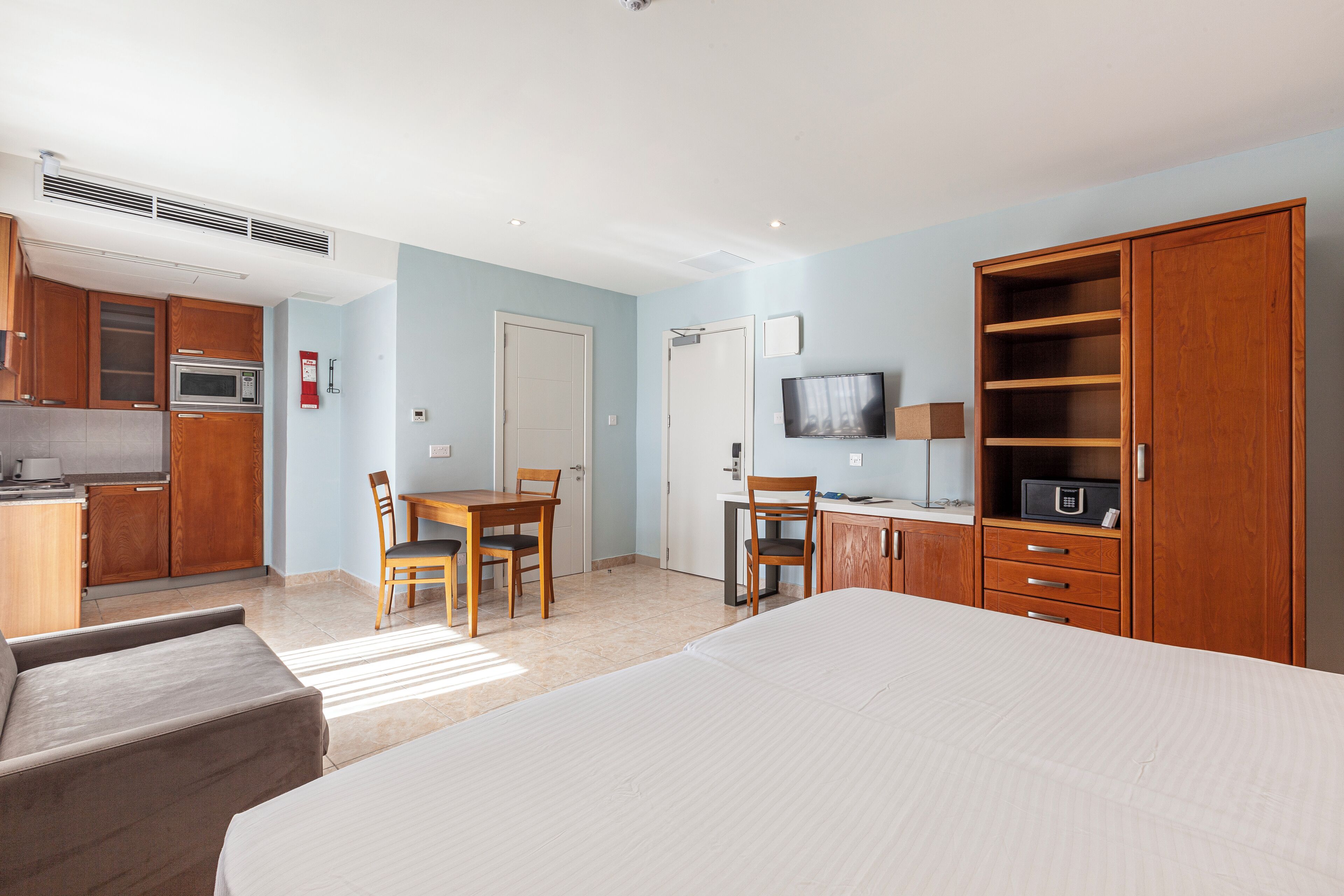 Quarto de hotel com cama, escrivaninha com cadeira, televisão, micro-ondas e guarda-roupa.