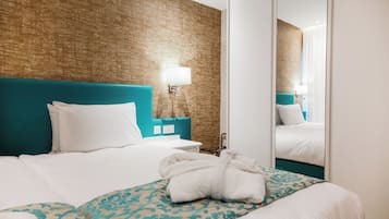 Quarto de hotel com cama, mesa de cabeceira, espelho e banheiro visível por uma porta aberta.