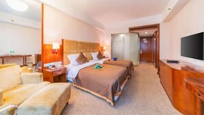 Quarto de hotel com duas camas, uma mesa, televisão e área de recepção.