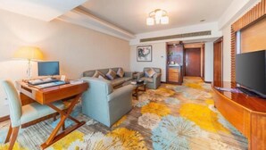 Quarto de hotel com sofá, escrivaninha com abajur, televisão de tela plana e carpete estampado.