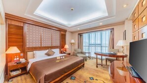 Quarto de hotel com uma cama grande, uma escrivaninha, uma televisão e vista para a cidade.