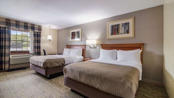 Quarto de hotel com duas camas, janela com cortinas, escrivaninha com abajur e quadros nas paredes.