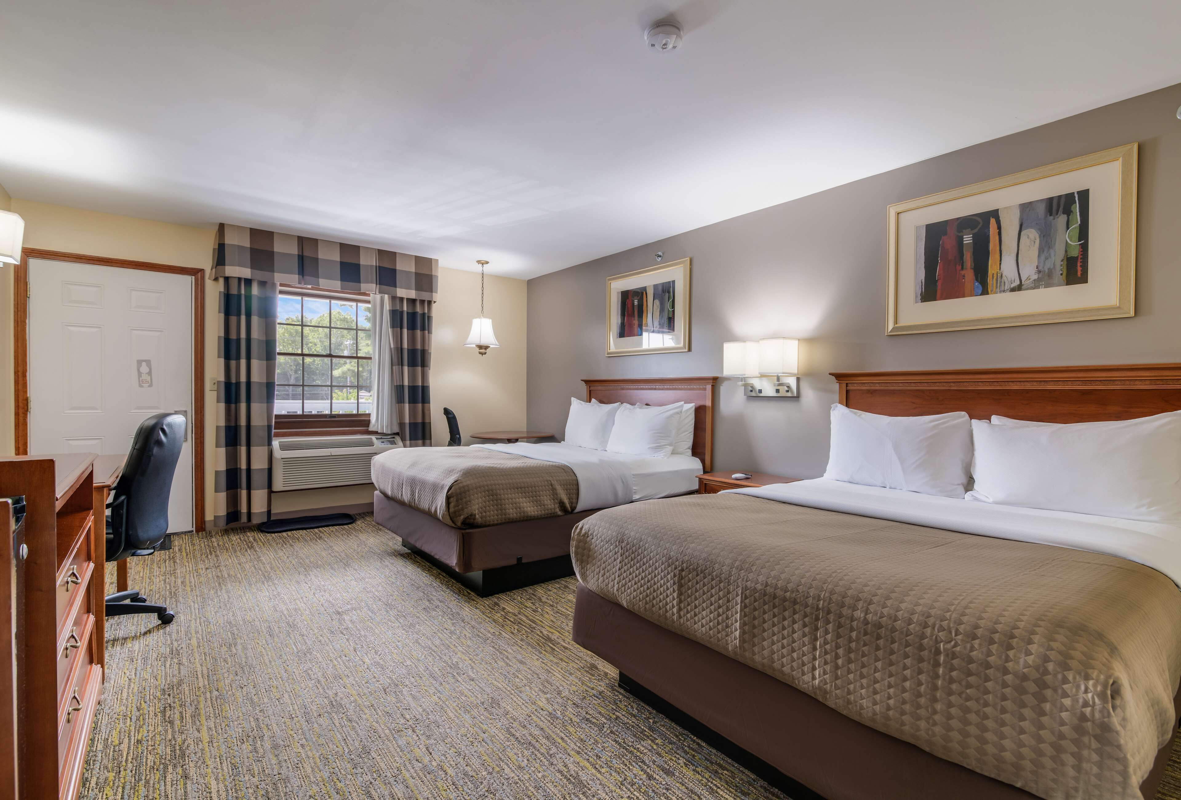 Quarto de hotel com duas camas, uma escrivaninha, uma cadeira e uma janela com cortinas.
