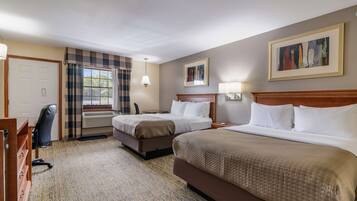 Quarto de hotel com duas camas, uma escrivaninha, uma cadeira e uma janela com cortinas.
