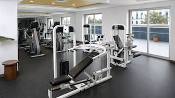 Academia com diversos equipamentos de exercício, amplas janelas e design moderno e limpo.