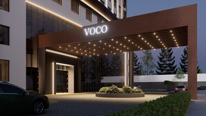 Entrada de hotel com design moderno, área coberta com iluminação e jardim ajardinado.