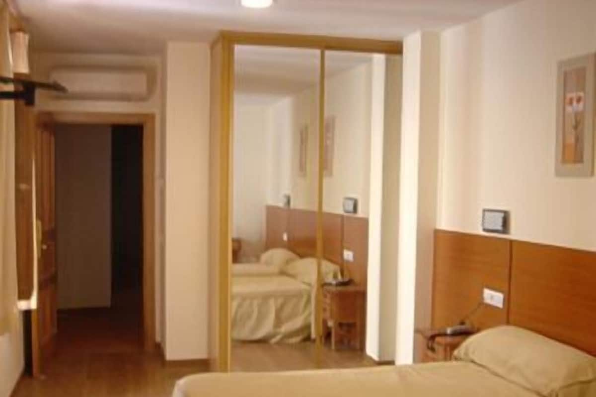 Quarto de hotel com duas camas, piso de madeira, um espelho e uma mesinha de cabeceira.