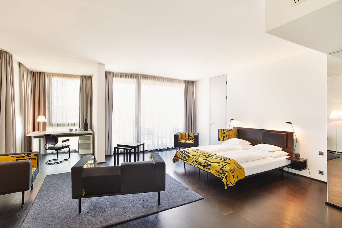 Quarto de hotel moderno com cama, escrivaninha e área de estar.