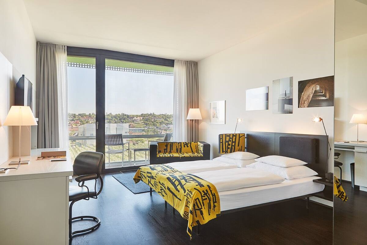 Quarto de hotel com cama, escrivaninha, cadeira e vista da cidade.