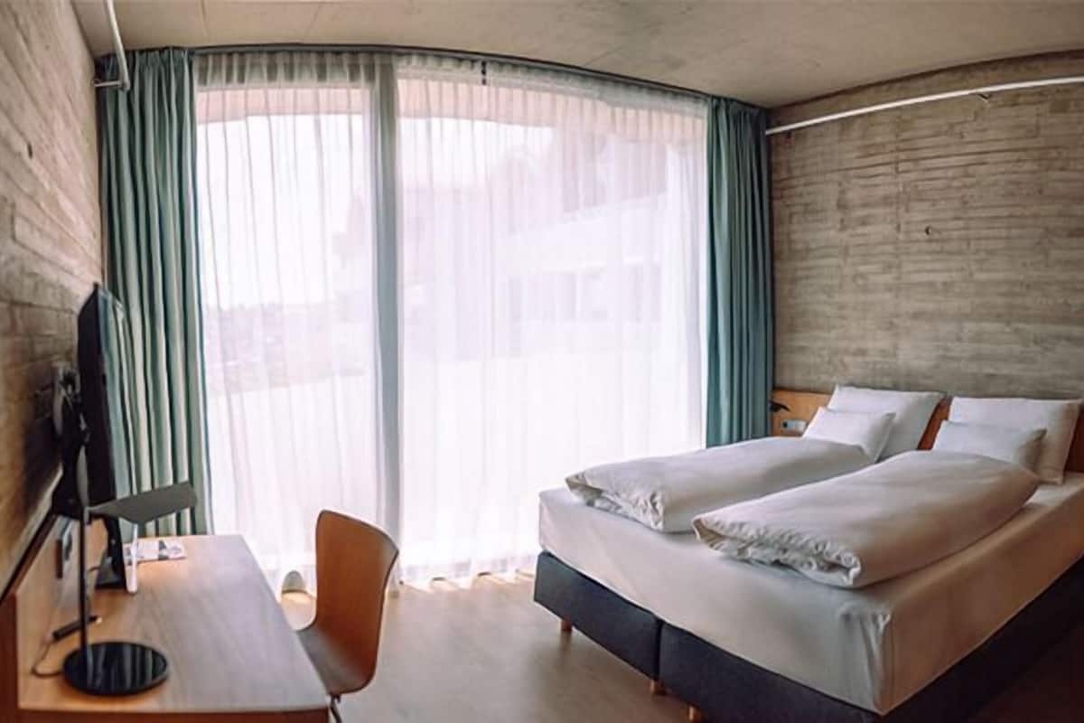 Quarto de hotel moderno com uma cama grande, uma escrivaninha e uma cadeira.