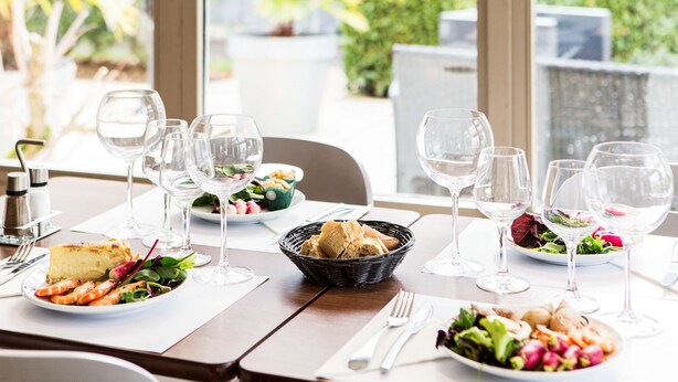 Uma mesa de jantar posta com pratos de comida, copos de vinho e talheres.