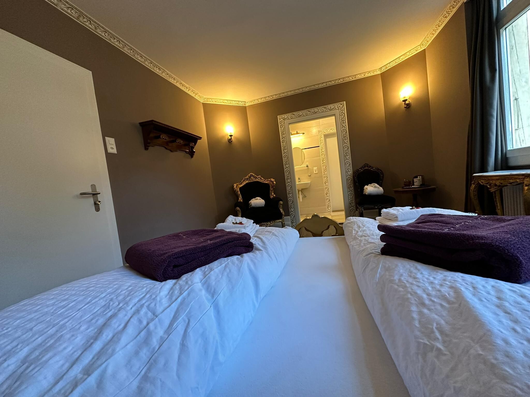Quarto de hotel com duas camas, um espelho grande e vista para o banheiro.