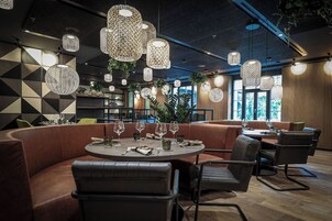Interior moderno de restaurante com mesas redondas, assentos de couro e luminárias decorativas penduradas.