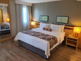 Quarto de hotel com uma cama grande, duas mesas de cabeceira com luminárias, um espelho e duas obras de arte emolduradas na parede.