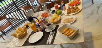 Uma mesa de café da manhã com diversos alimentos, uma cafeteira e uma garrafa de suco.
