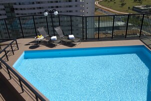 Piscina no terraço com duas espreguiçadeiras e uma mesa, cercada por um corrimão preto.