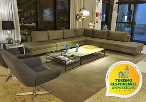Uma sala de estar moderna com um sofá seccional, uma mesa de centro de vidro e uma poltrona cinza.