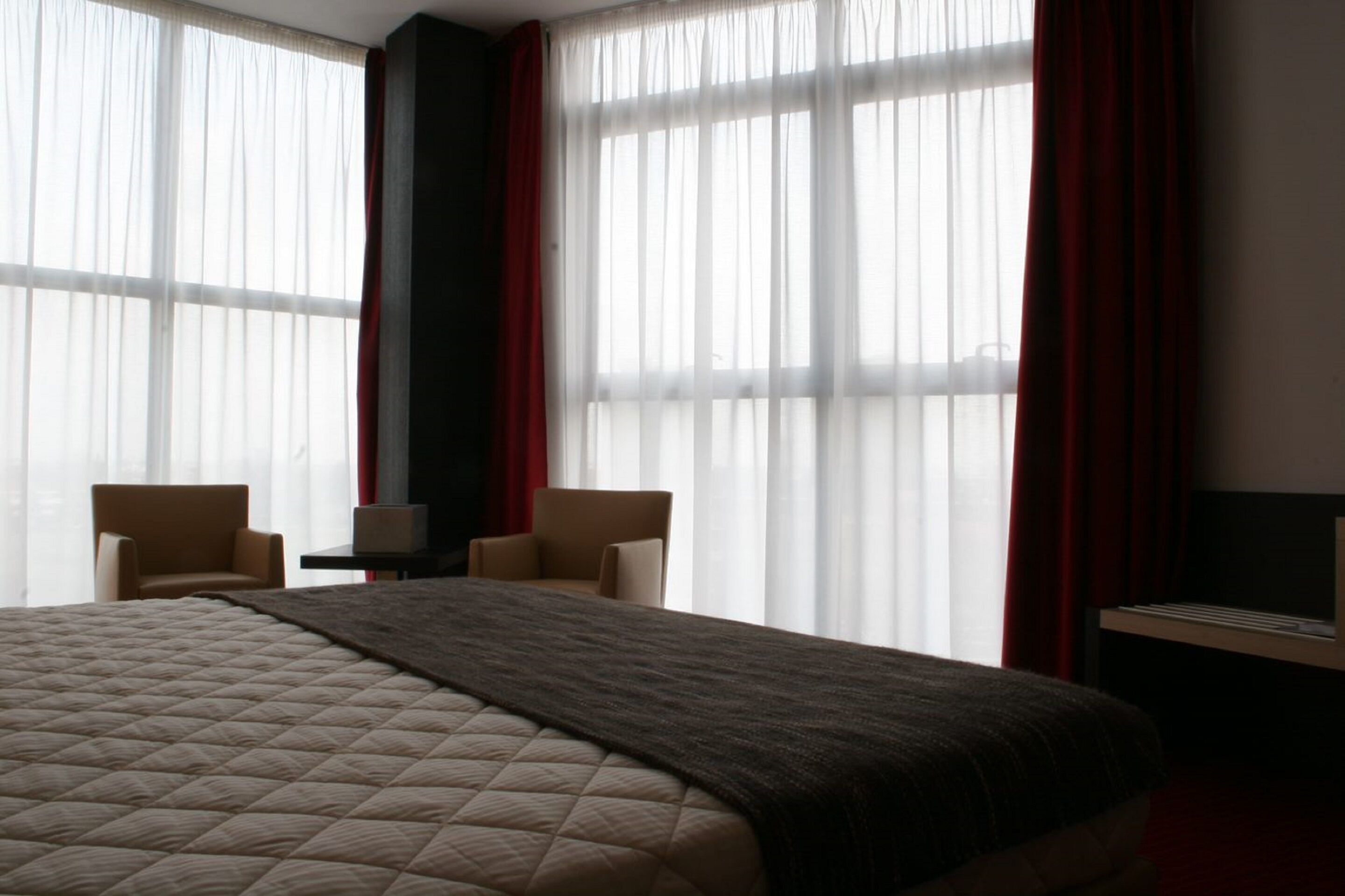 Quarto de hotel com uma cama grande, duas cadeiras, uma mesinha e uma televisão.