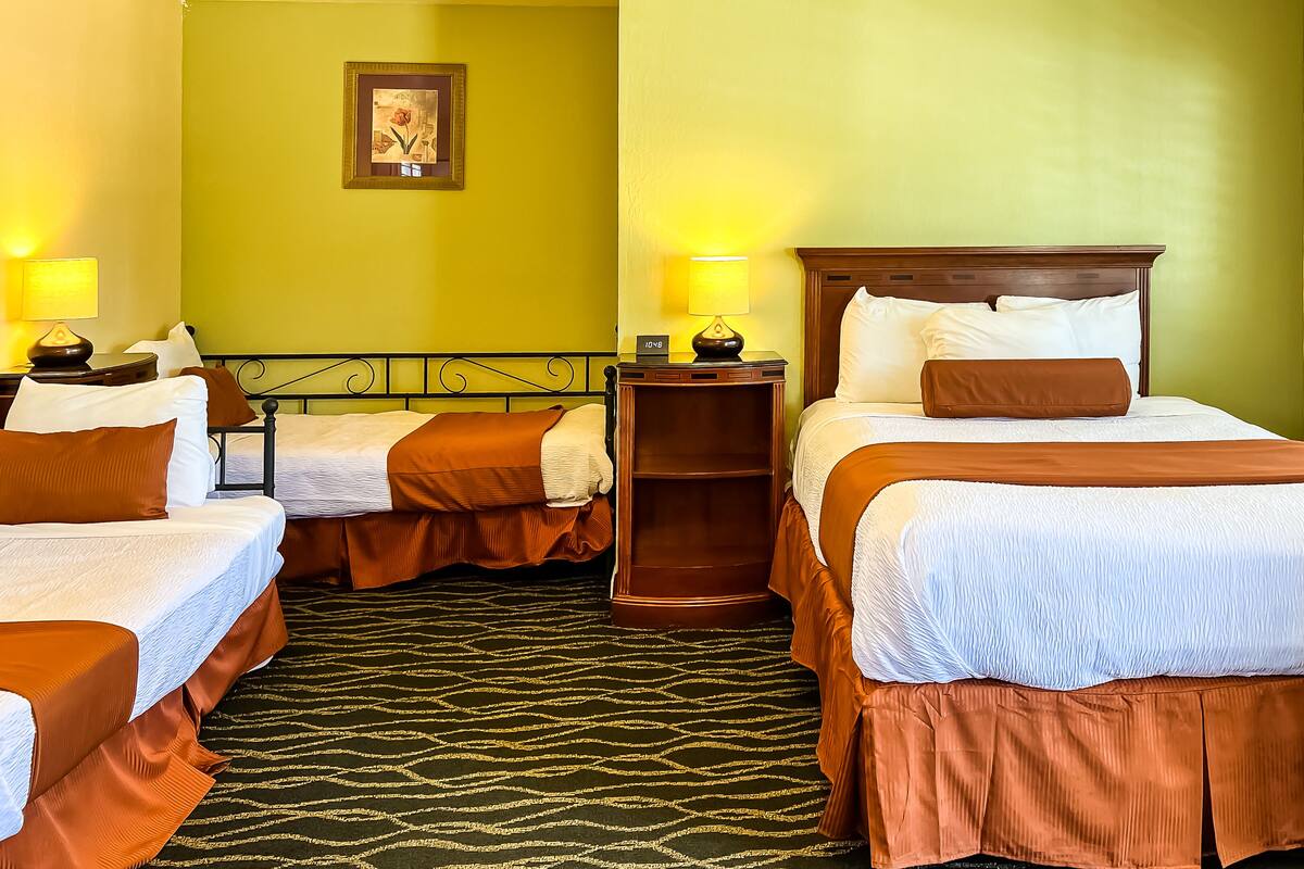 Quarto de hotel com duas camas de solteiro, mesa de cabeceira com luminária, cabeceira de madeira e quadro pendurado na parede.