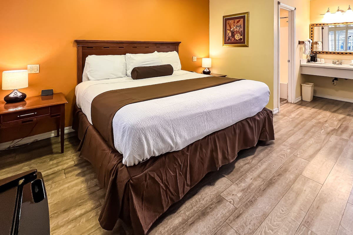 Quarto de hotel com cama grande, mesa de cabeceira, escrivaninha e banheiro com pia e espelho.