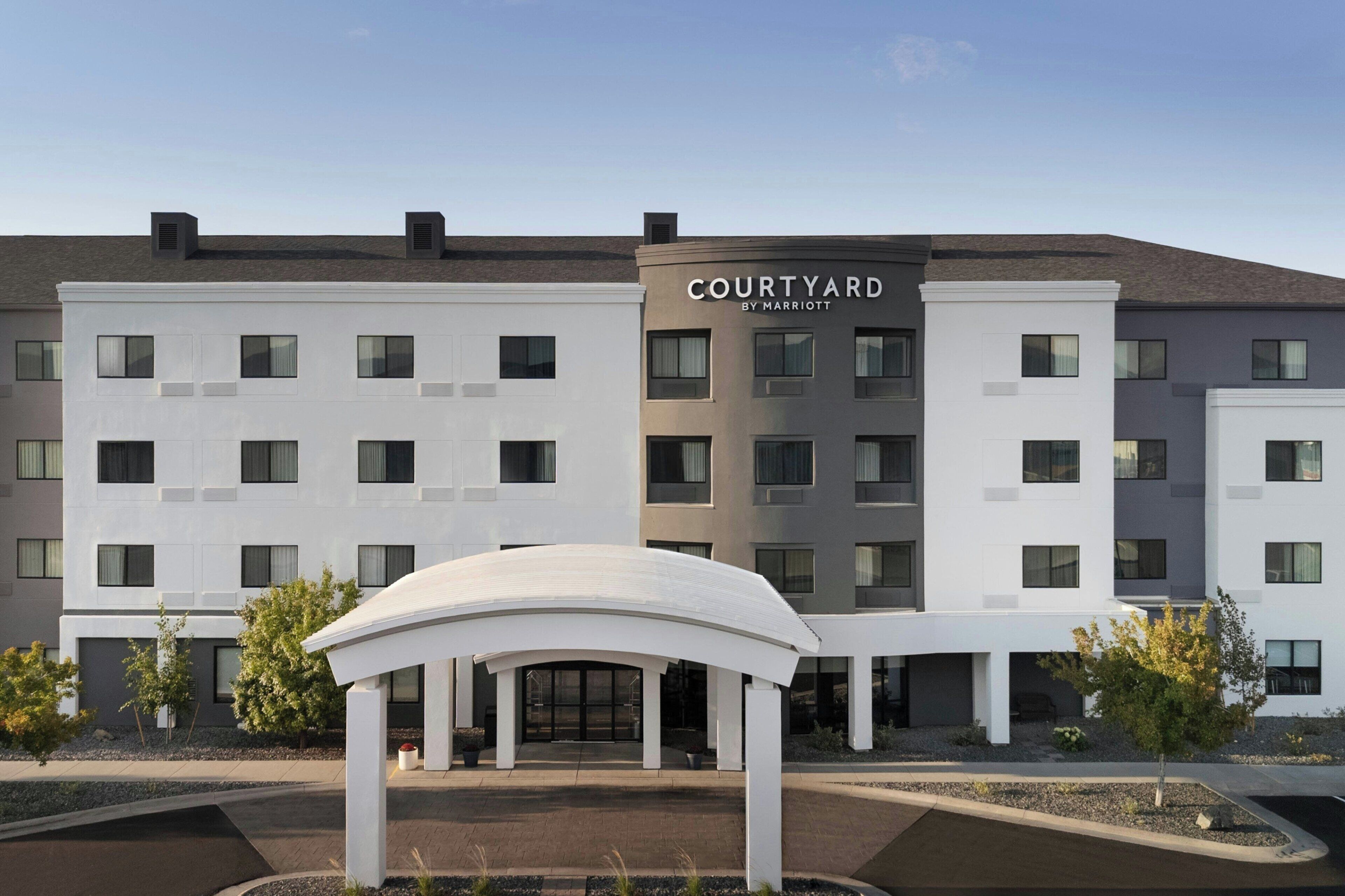 Um hotel Courtyard by Marriott com design moderno, apresentando um pátio central com toldo branco, vários andares e telhado plano.