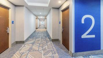 Um corredor de hotel com carpete estampado, portas de madeira e parede azul com o número 2.