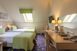Quarto de hotel com duas camas, uma escrivaninha com telefone, uma cadeira e uma mesinha de centro com uma chávena e um copo.