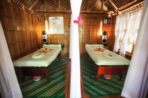 Um quarto com duas mesas de massagem, paredes de madeira, um esquema de reflexologia manual e um relógio.