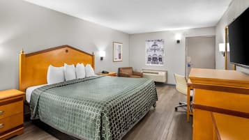 Quarto de hotel com cama de madeira, uma mesa, uma cadeira, uma televisão e um cartaz na parede.