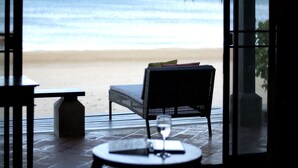 Uma cadeira de vime com almofadas numa varanda com vista para a praia.