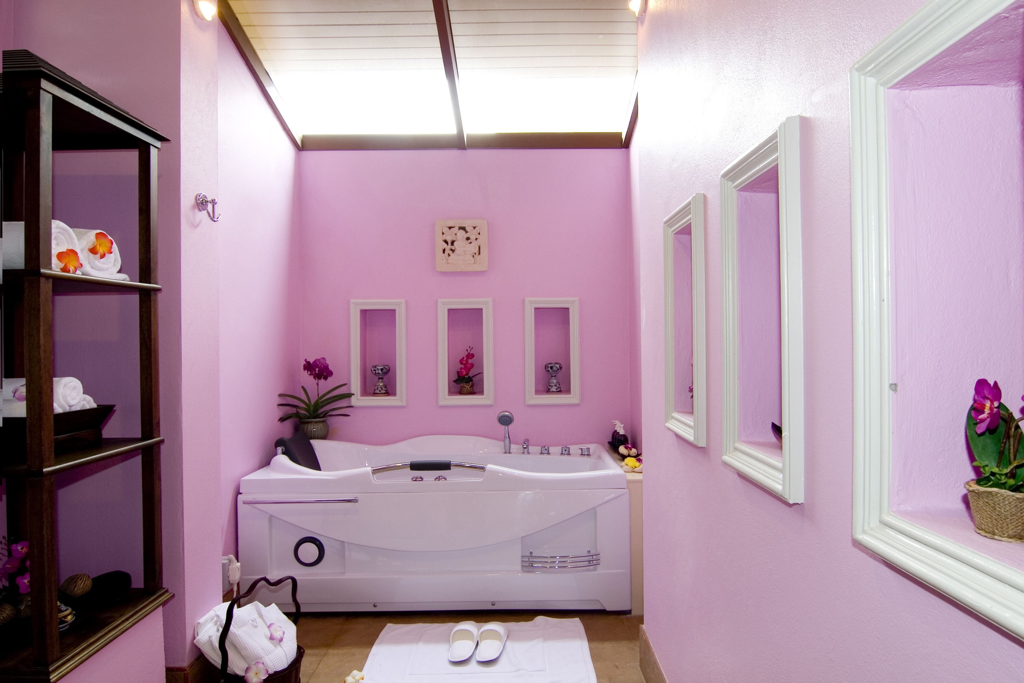 Uma casa de banho em tons de rosa, com banheira, prateleiras com toalhas e quadros nas paredes.