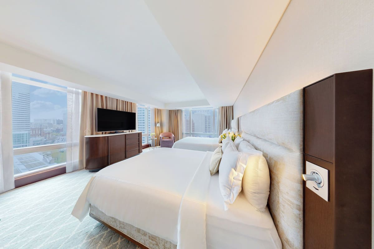 Quarto de hotel moderno com uma cama grande, televisão de tela plana, escrivaninha e vista para a cidade.