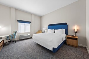 Quarto de hotel com cama grande, escrivaninha, cadeira, aquecedor, janela com persianas e abajur.