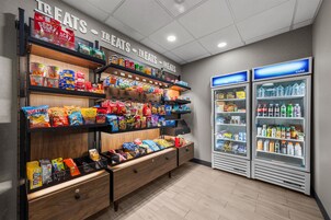 Uma seção de lanches com diversos produtos embalados e um refrigerador com água e refrigerantes.